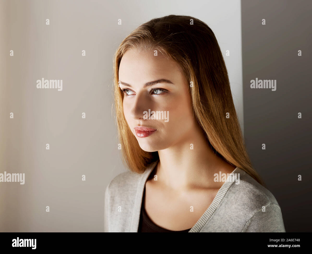 Dreaming woman standing near window in sunbeams. Portrait of blond ...