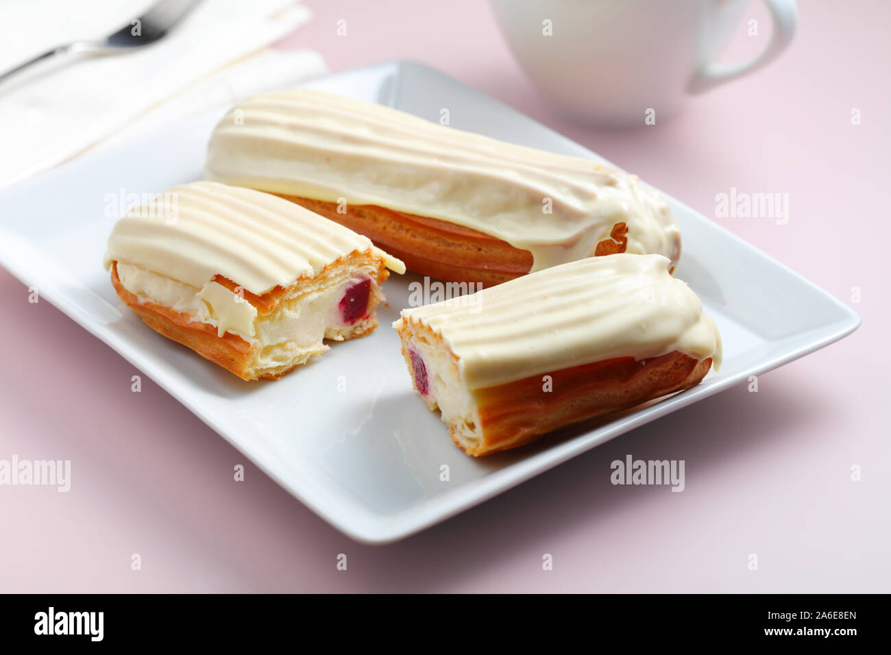 Eclairs with White Chocolate Glaze in a dish on pink background. One of ...