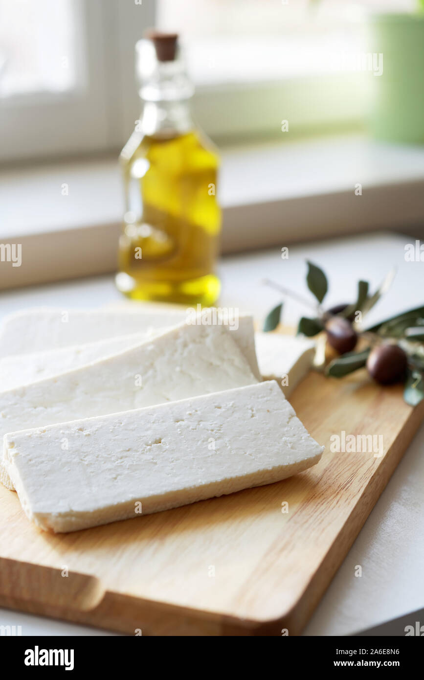 Sliced feta cheese on a cutting board, jug of olive oil, and olives on ...