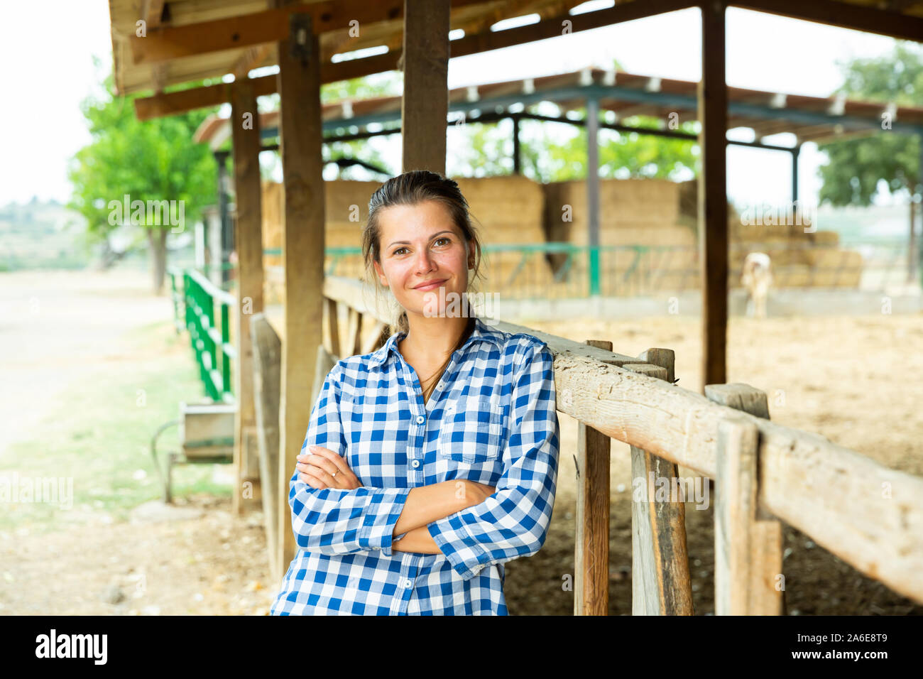 Happy confident young woman owner of ranch posing near empty stable on ...