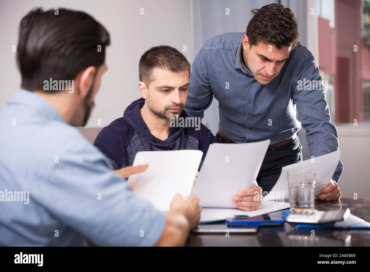 Three men having problems with some documents, worriedly discussing at ...