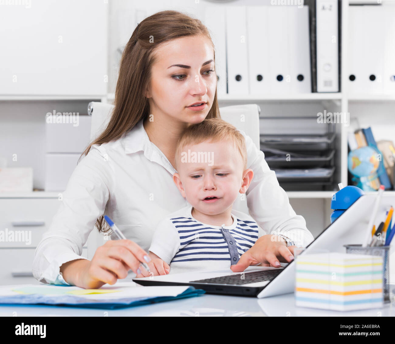 Woman 22-27 years old is working behind laptop with child in office ...