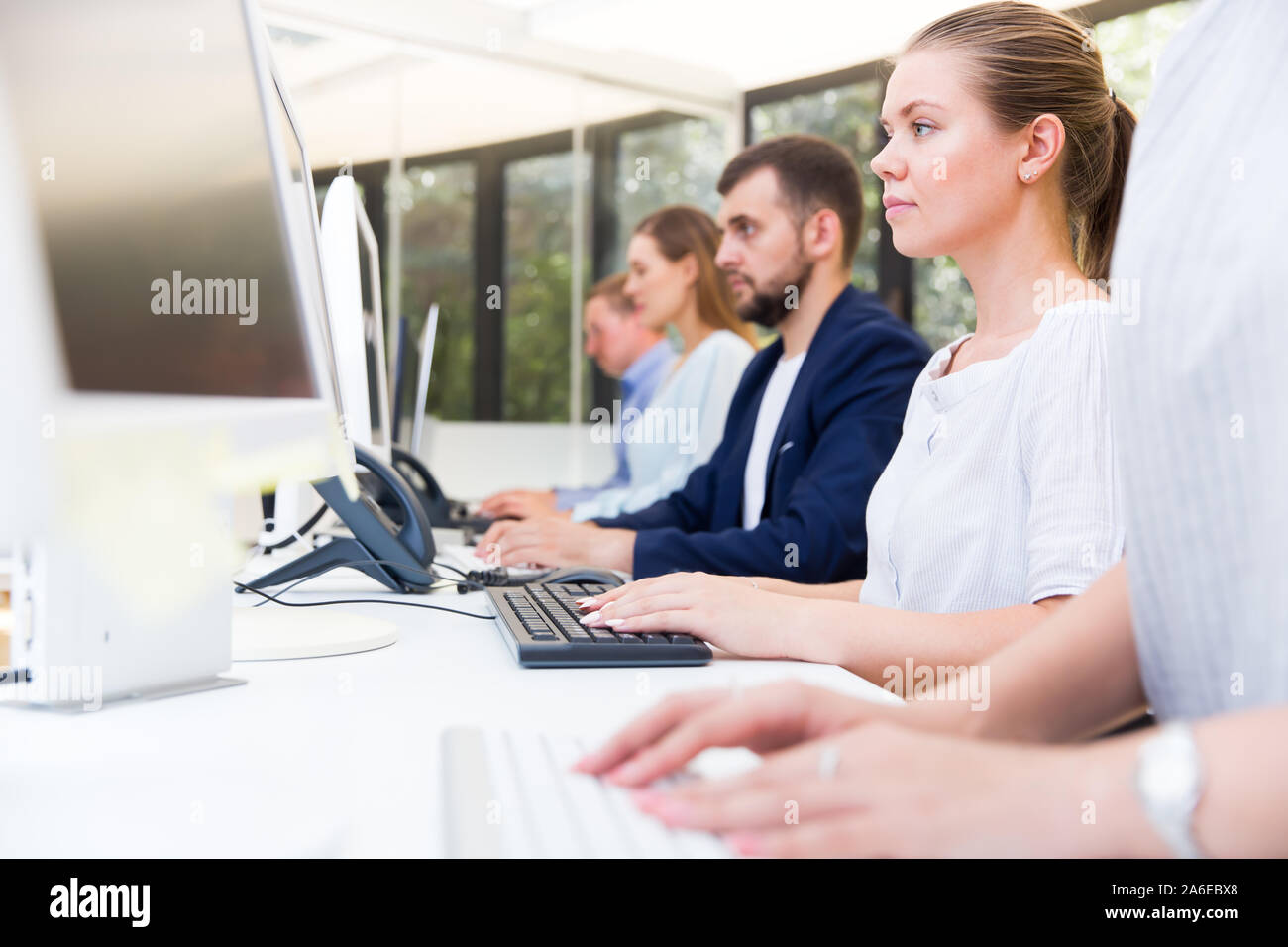 Side view of row of business people working with computers in modern ...