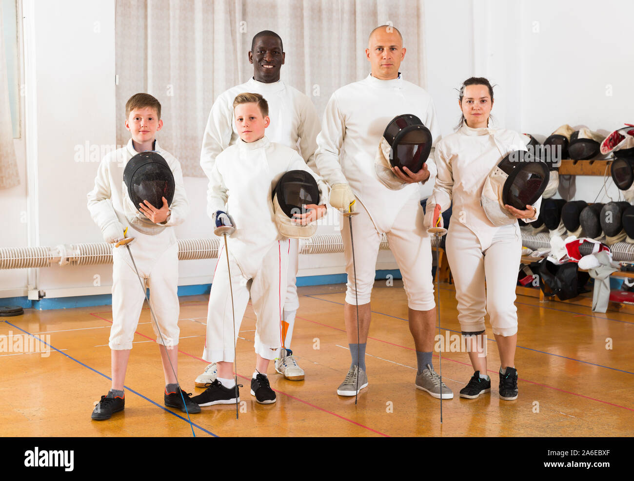 Portrait of happy mixed age group of athletes with foils at fencing ...