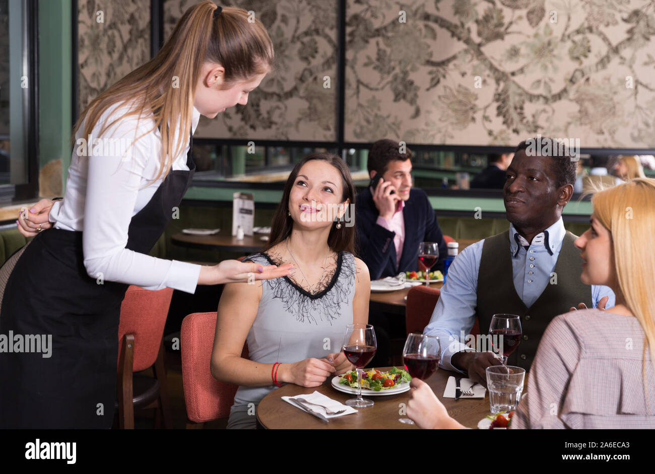 Positive elegant company of three sitting at restaurant table, talking ...