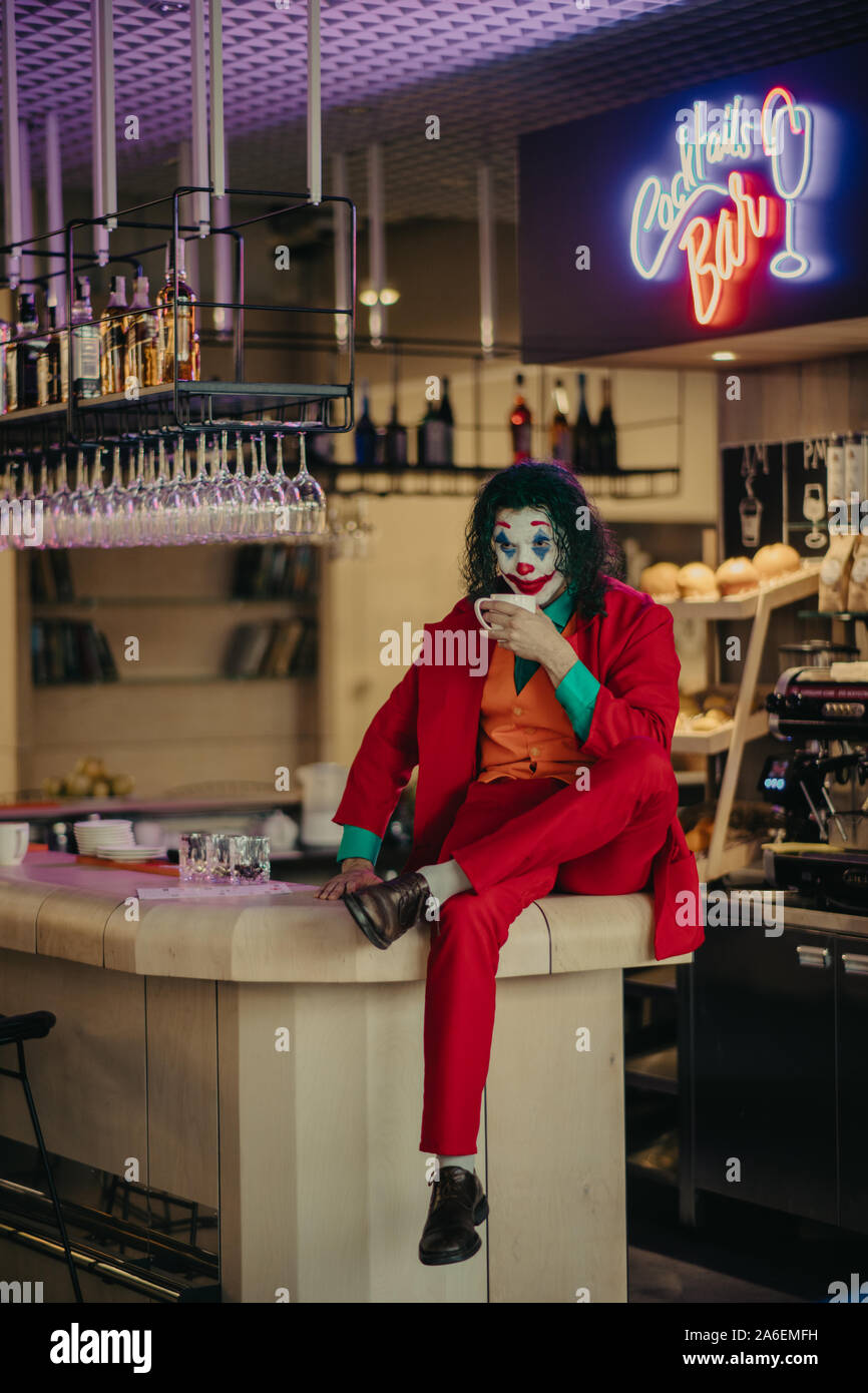 Cosplayer portrays a crazy clown and drinks coffee against the ...