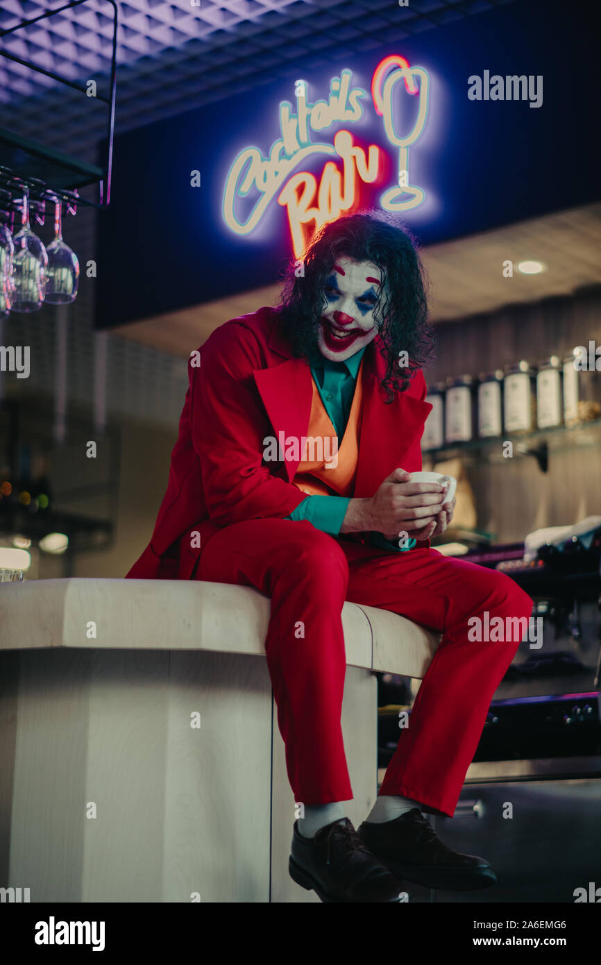 Cosplayer portrays a crazy clown and drinks coffee against the ...