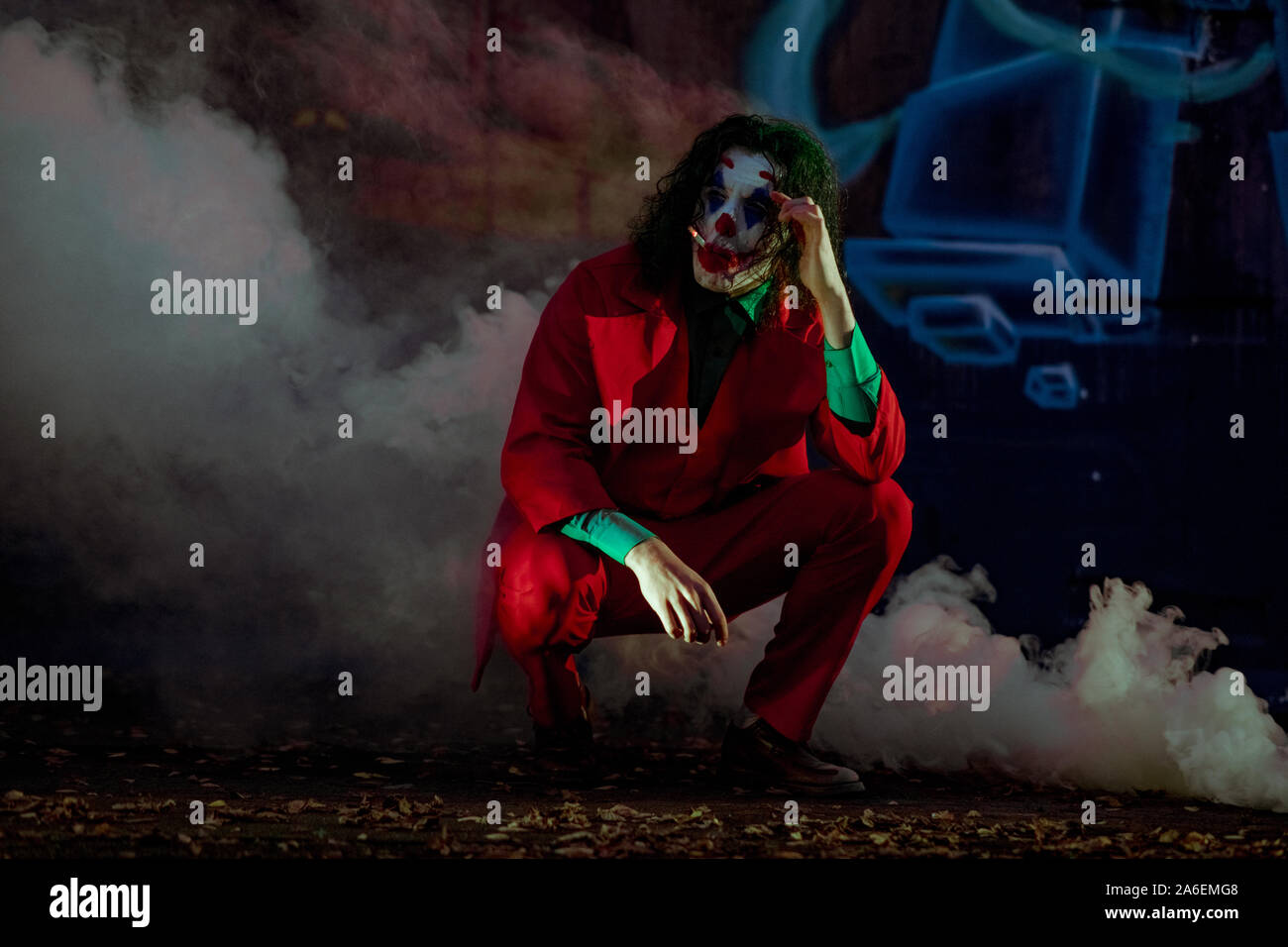 Cosplayer in the image of a crazy clown smokes a cigarette against ...