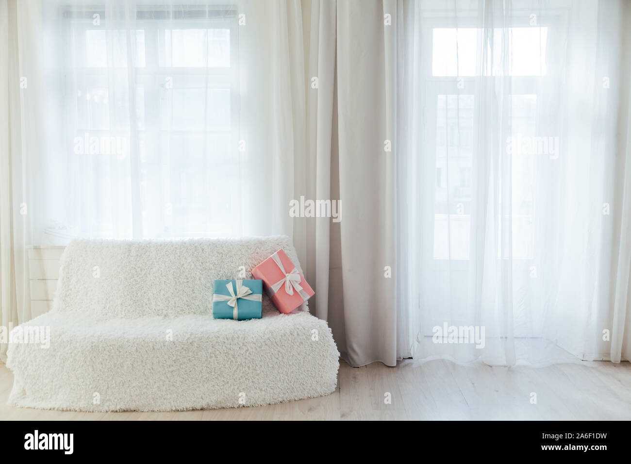 white sofa with gifts in the interior of the white room with windows ...