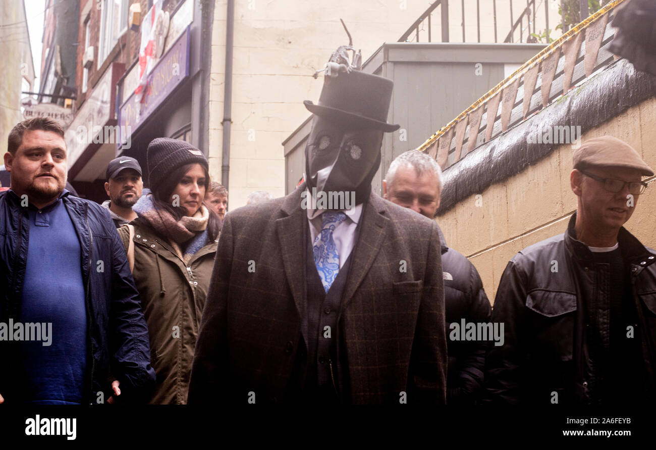 Man wearing mask and traditional Goth costume followed by friends ...