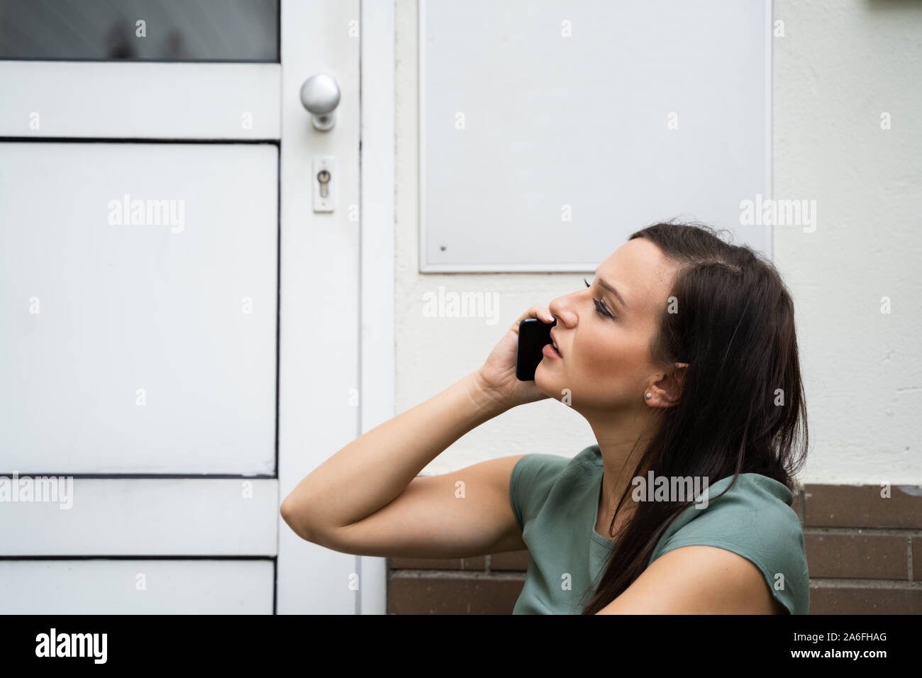 An Afraid Young Woman Sitting Outside The Door Talking On Mobilephone ...