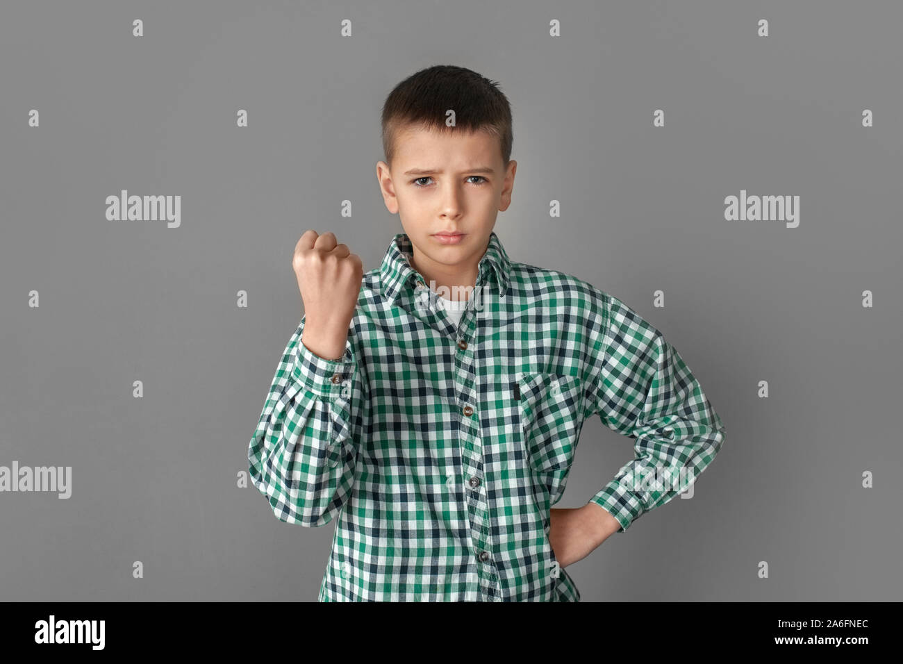 Freestyle. Boy standing isolated on grey wall showing fist menacingly ...