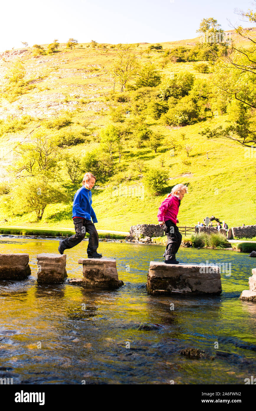 A little boy and girl hoping, jumping over the Dovedale stepping stones ...