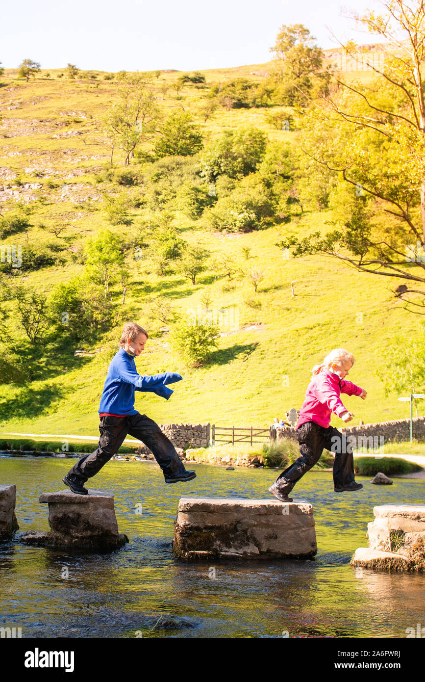 A little boy and girl hoping, jumping over the Dovedale stepping stones ...