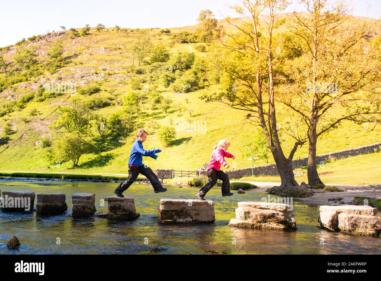 A little boy and girl hoping, jumping over the Dovedale stepping stones ...