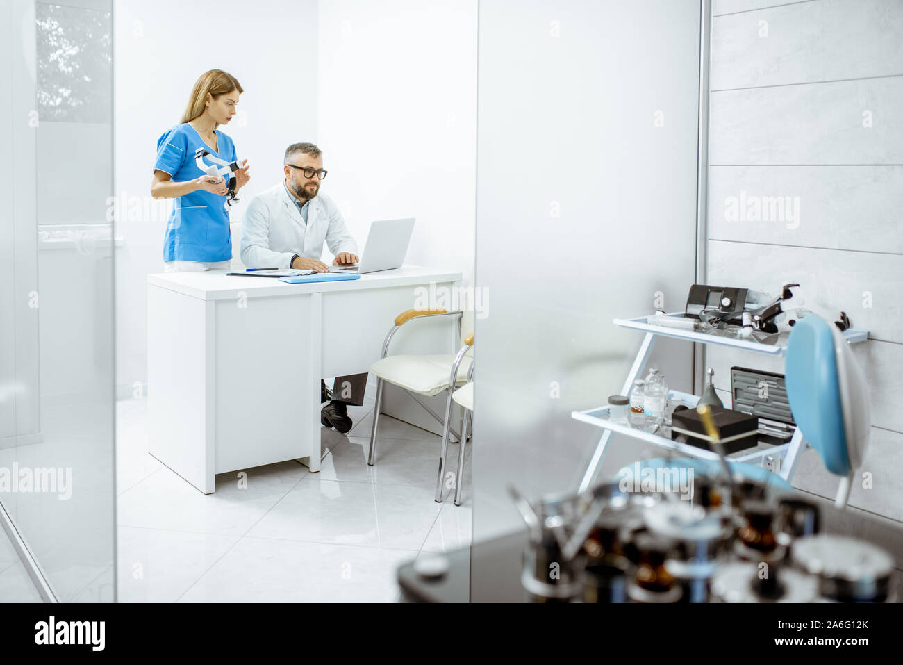 Senior otolaryngologist and female assistant working with laptop at the ...