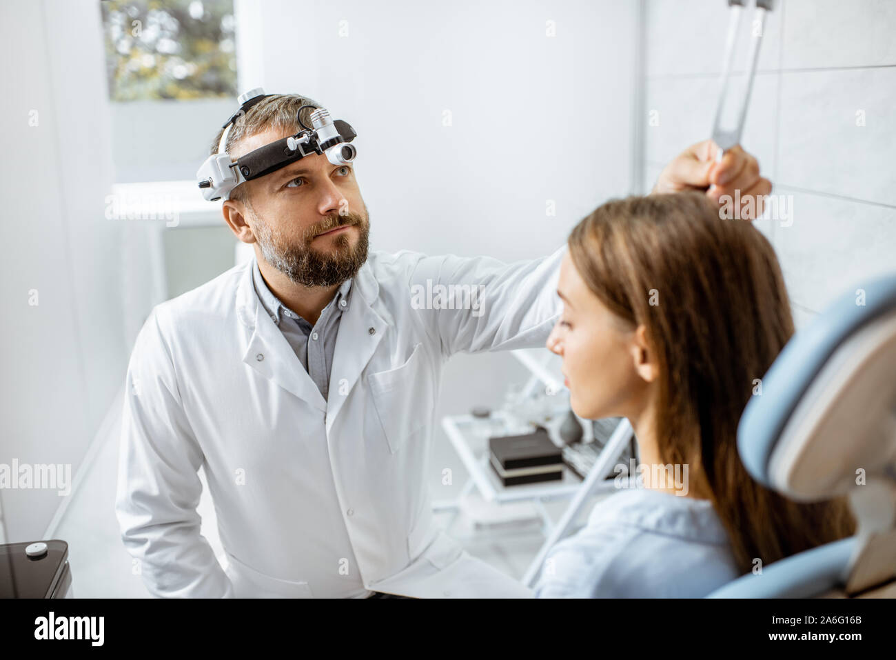 Senior otolaryngologist examining ears with ENT tuning fork for a young ...