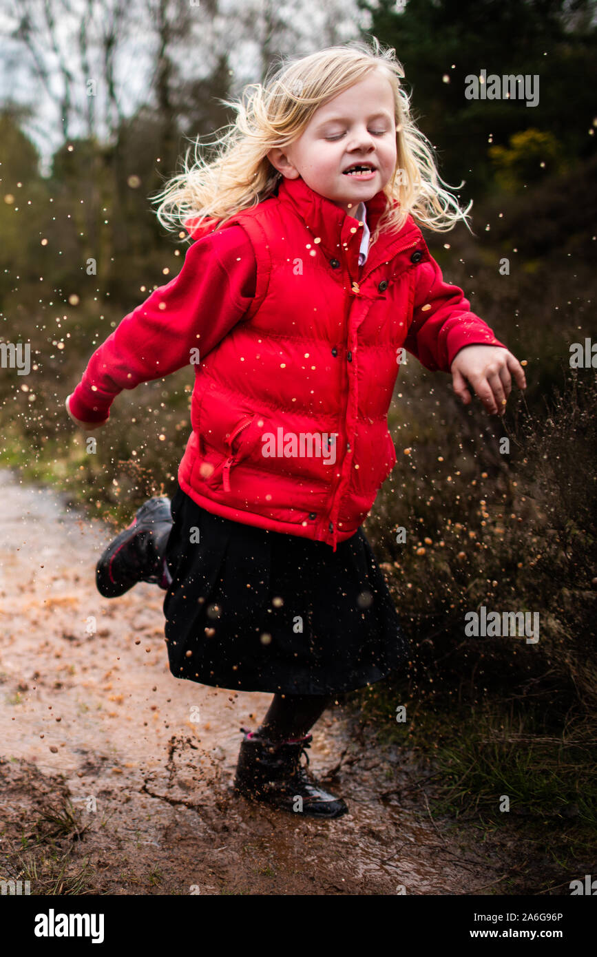 A little girl walks, runs and jumps through and into very muddy puddles ...