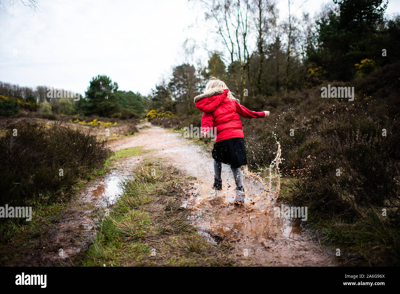 A little girl walks, runs and jumps through and into very muddy puddles ...