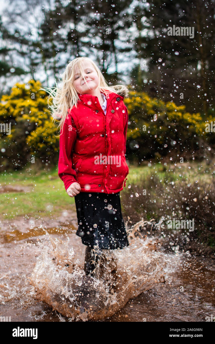 A little girl walks, runs and jumps through and into very muddy puddles ...