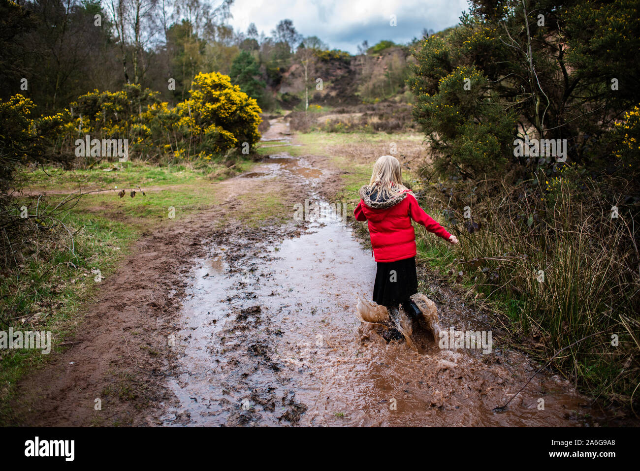 A little girl walks, runs and jumps through and into very muddy puddles ...