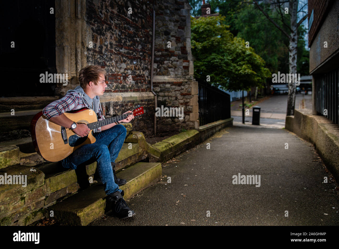 A handsome young man in a hat playing guitar and busking for money ...
