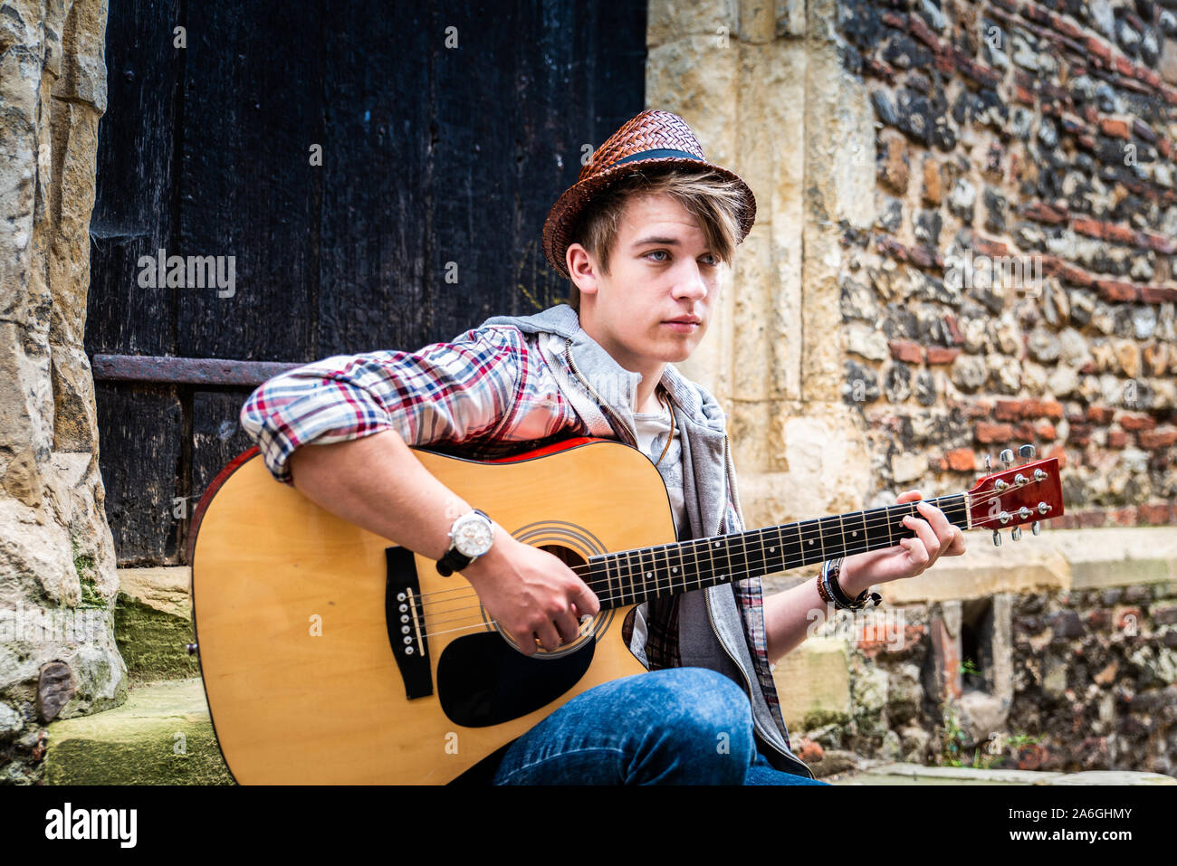 A handsome young man in a hat playing guitar and busking for money ...