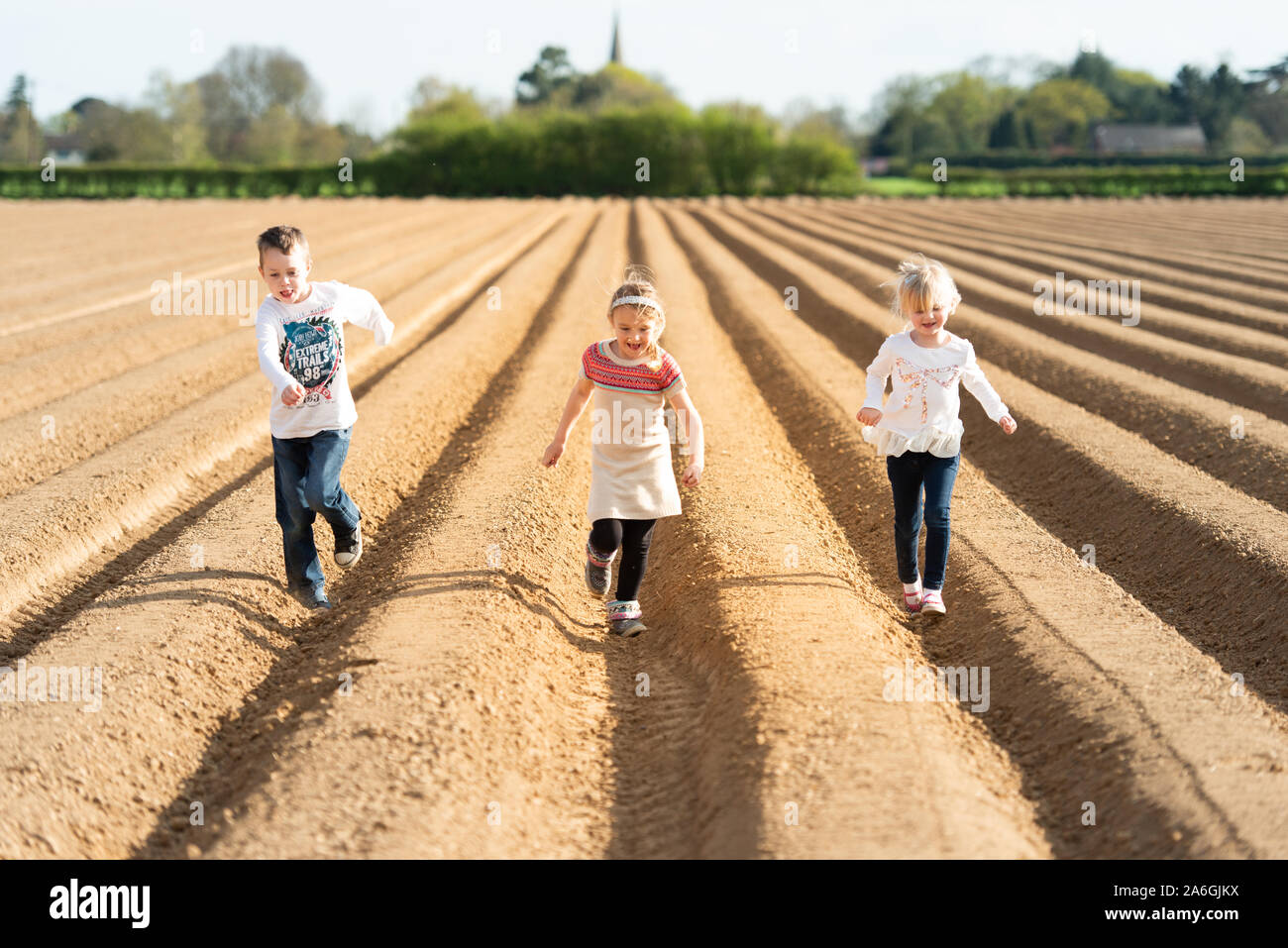 Three children run across a freshly ploughed, cropped farmers field ...