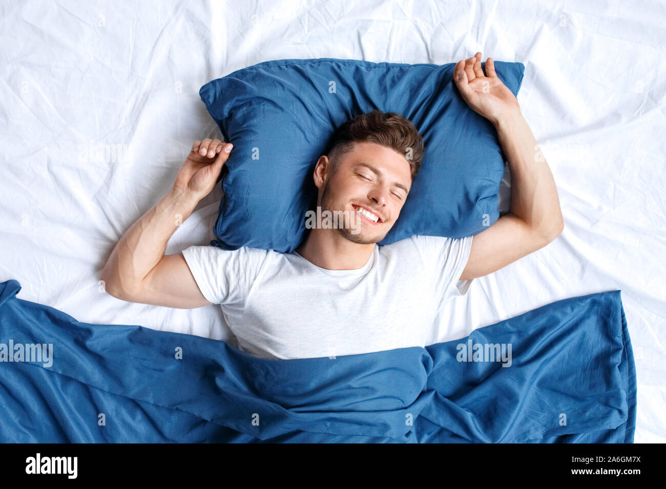 Bedtime. Guy lying on bed top view sleeping hands up happy Stock Photo ...
