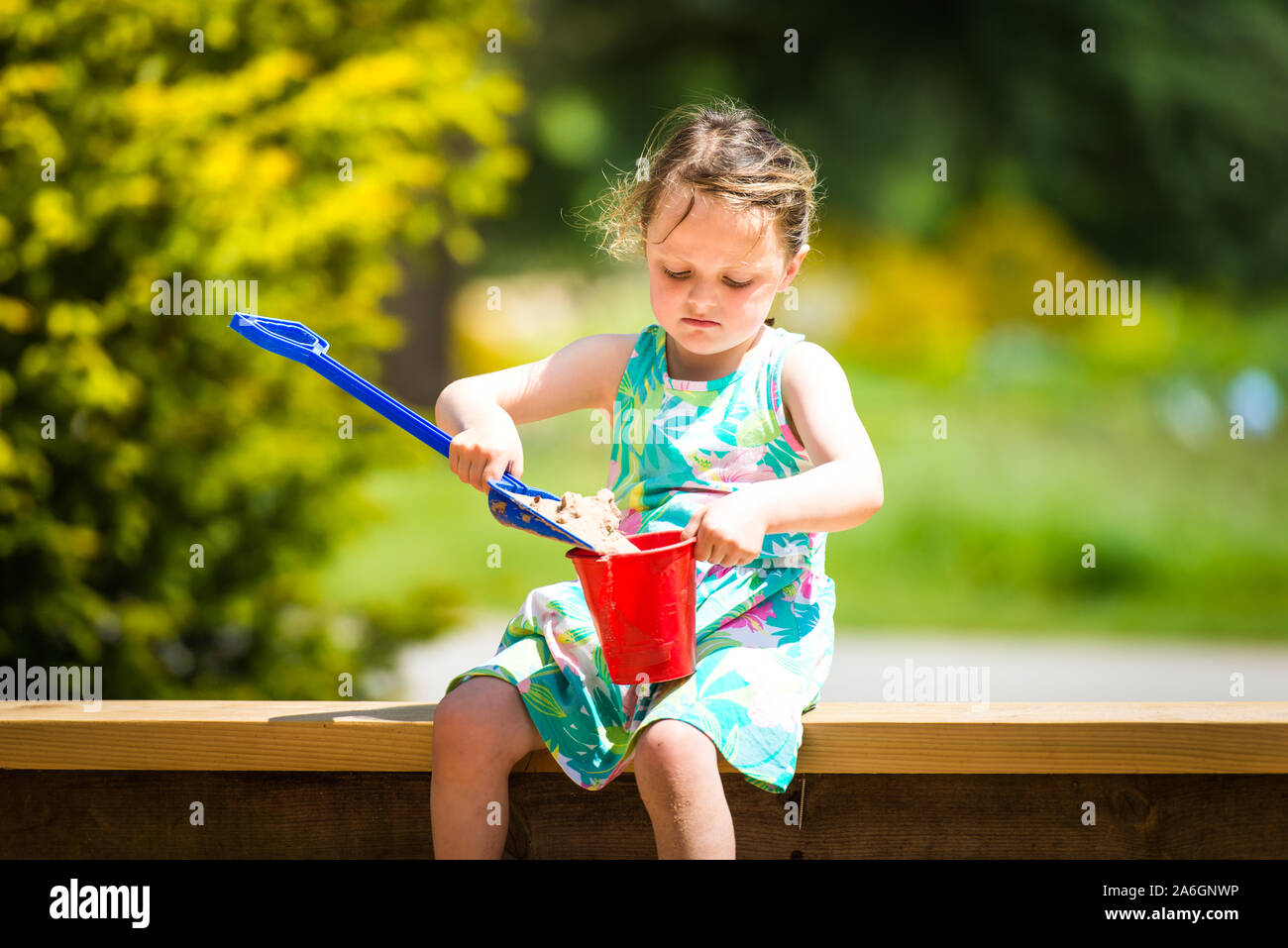 A cute little girl puts sand into a bucket ready for building ...