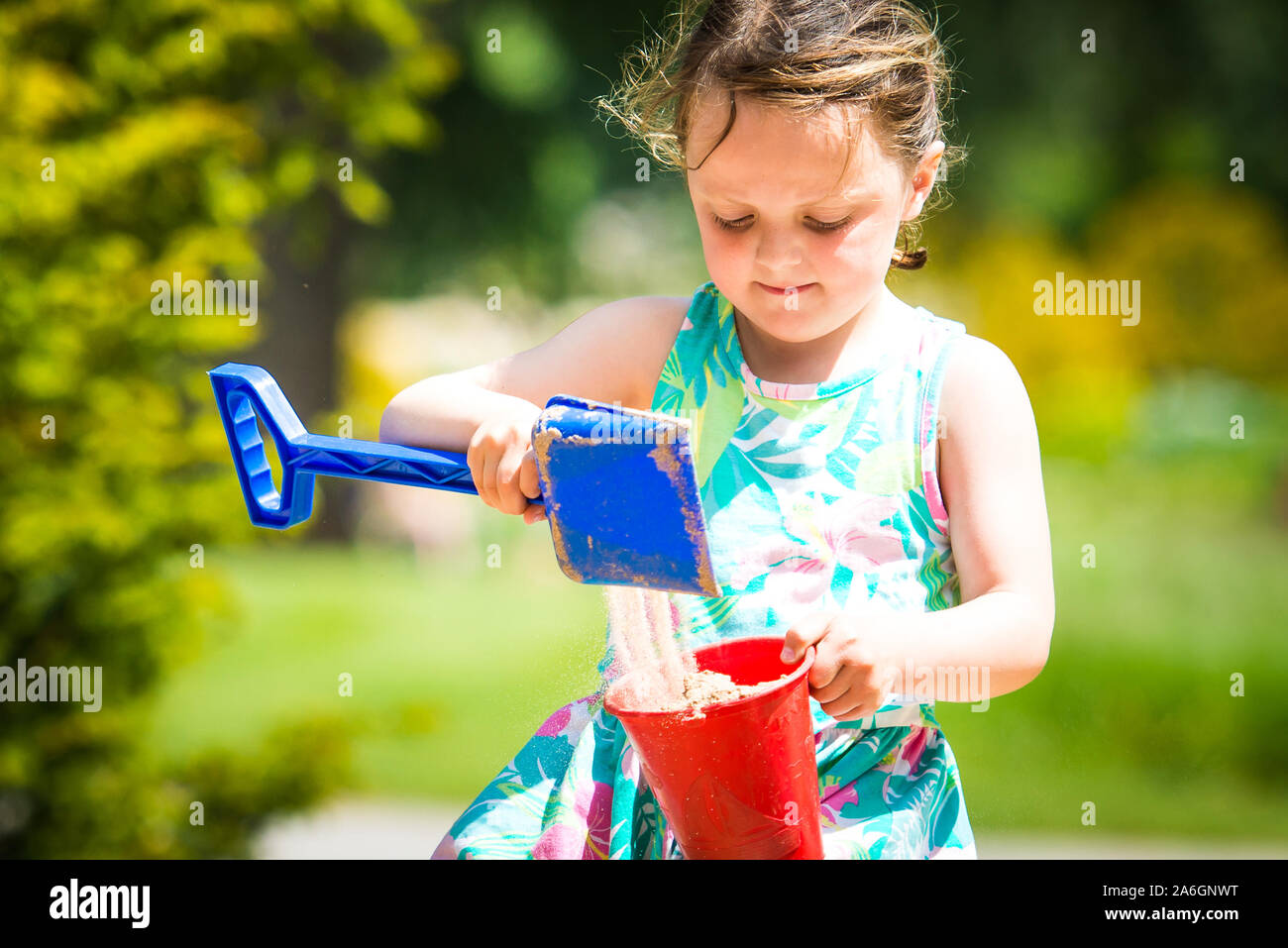 A cute little girl puts sand into a bucket ready for building ...