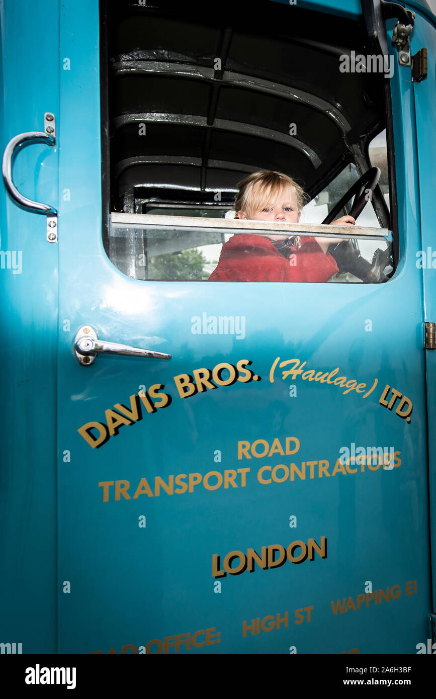 A cute, pretty little girl sits at the wheel of an old Davis Bros ...