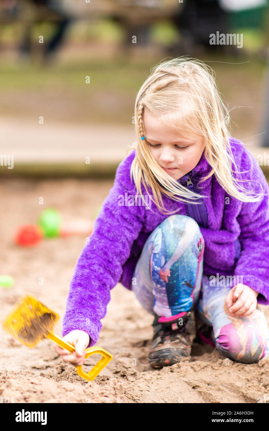 A pretty little girl plays in the sand pit, digging holes and making ...