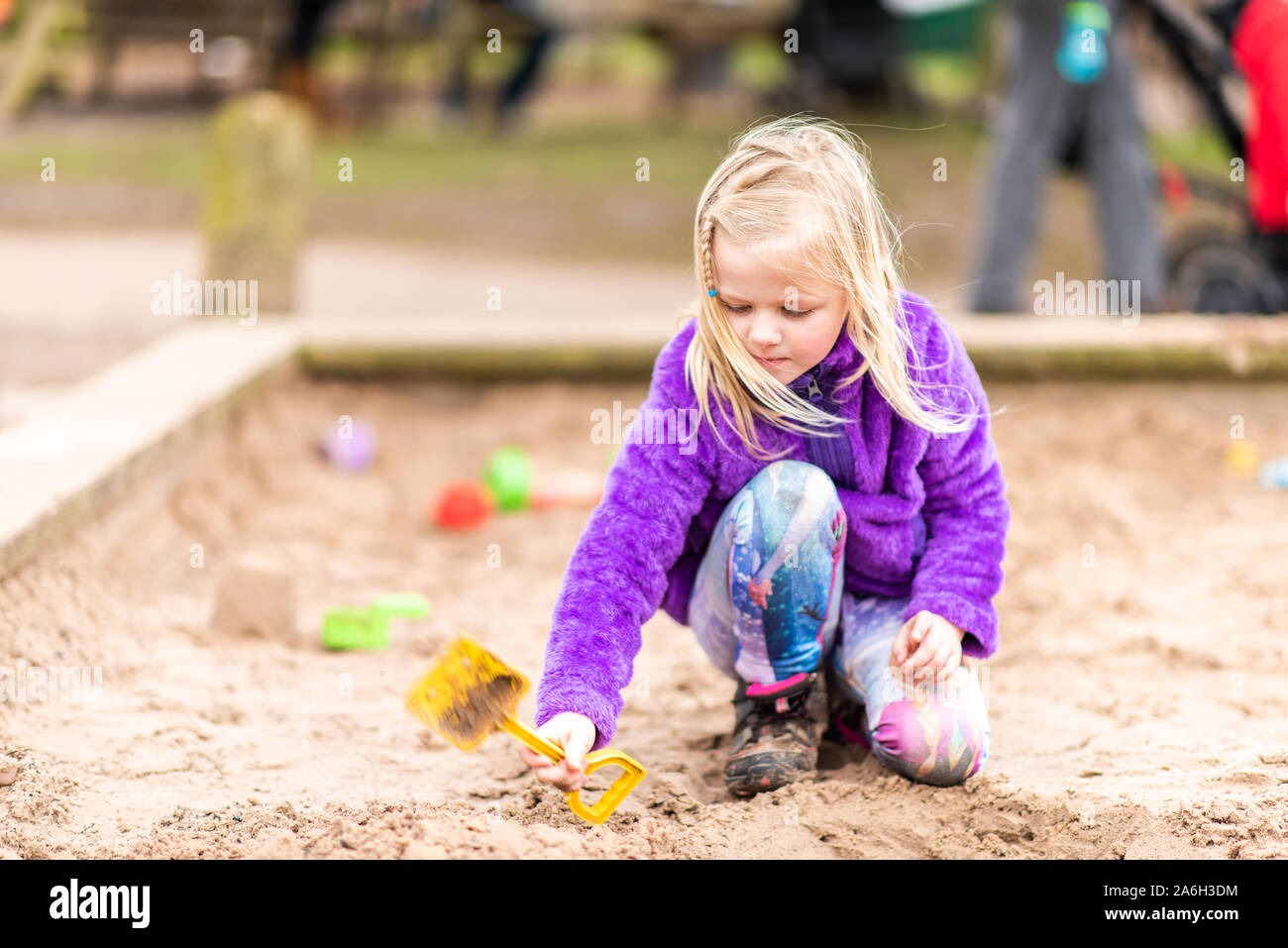 A pretty little girl plays in the sand pit, digging holes and making ...