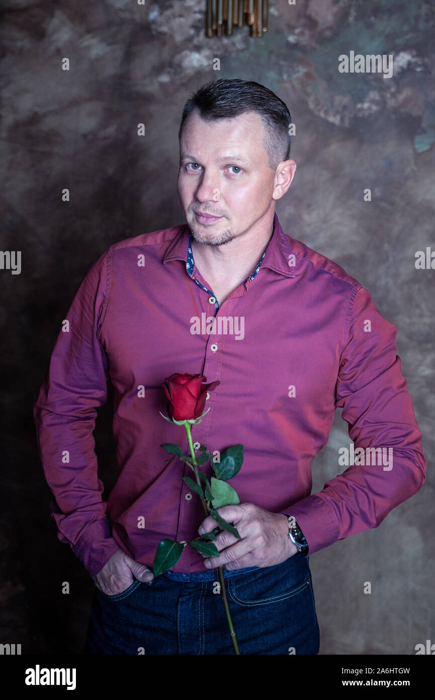 Pleasant white man with a red rose in his hands, looking at the camera ...