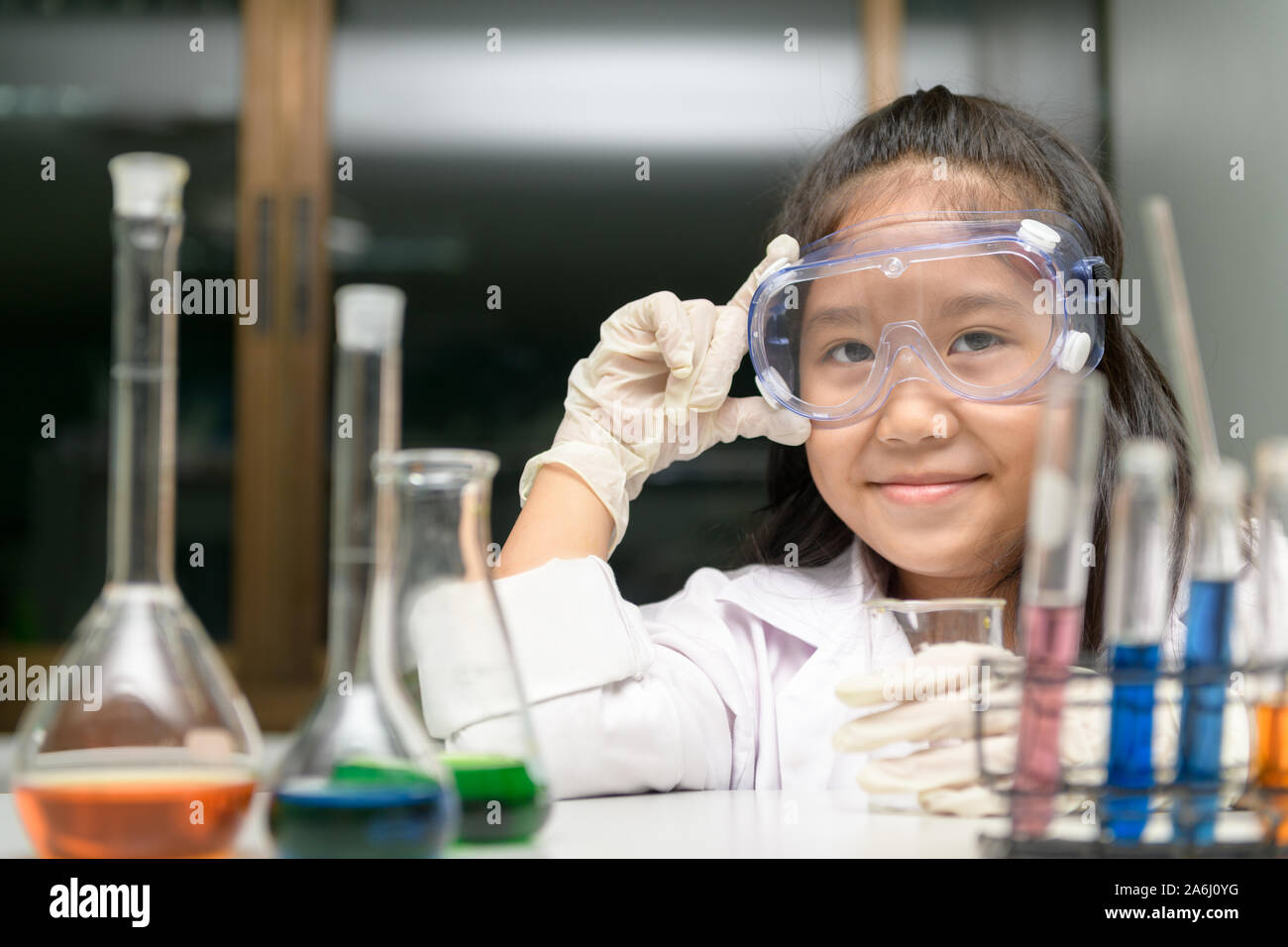 Cute little girl wearing safty goggle and lab coat making experiment in ...