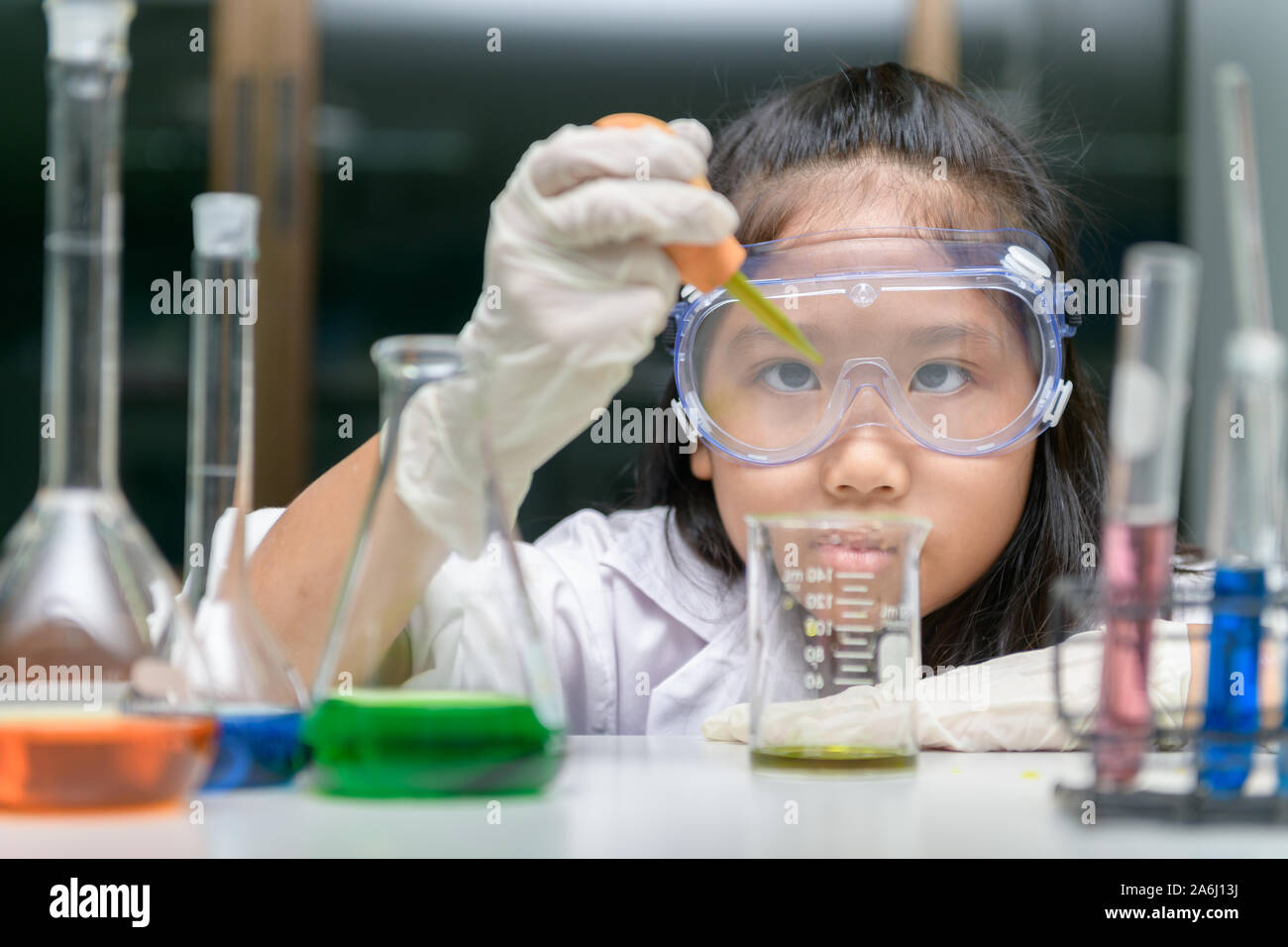 Cute little girl wearing safty goggle and lab coat making experiment in ...