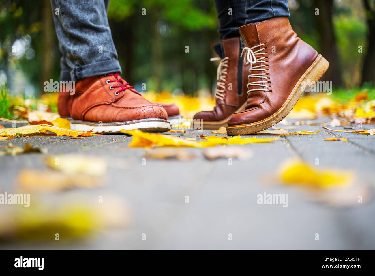 Feet of a couple in love in brown shoes on the path of the autumn park ...