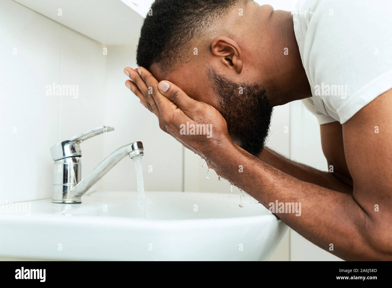 Black man washing his face, splashing water at sink in bathroom Stock ...