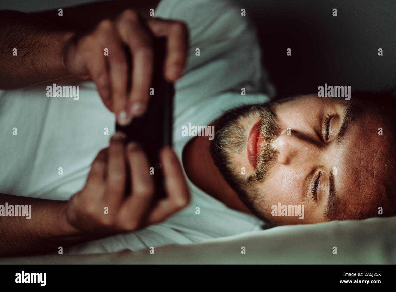 Young happy man cannot sleep and is watching something on his phone at ...