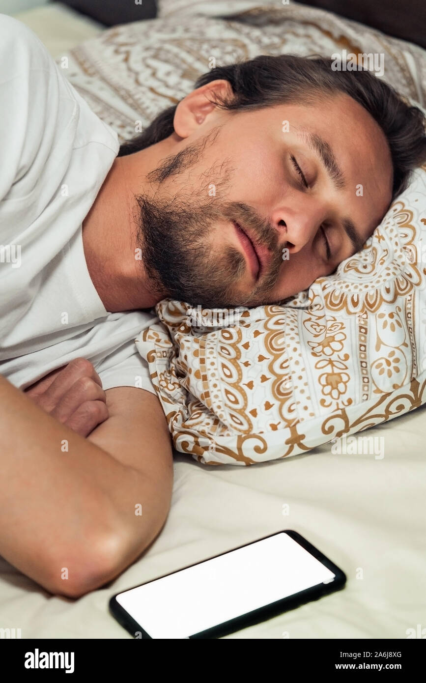 Phone in bed next to a handsome young man that is taking a nap. Phone's ...