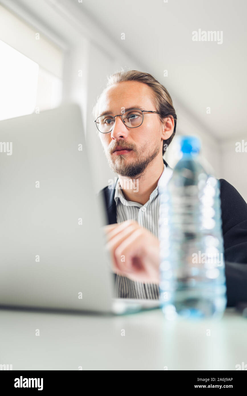 Photo of a handsome focused young man sitting by the desk and working ...
