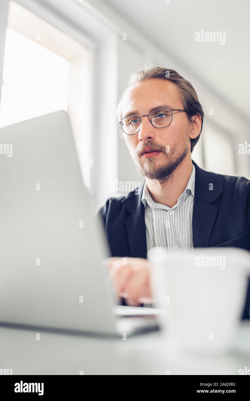 Photo of a handsome focused young man sitting by the desk and working ...