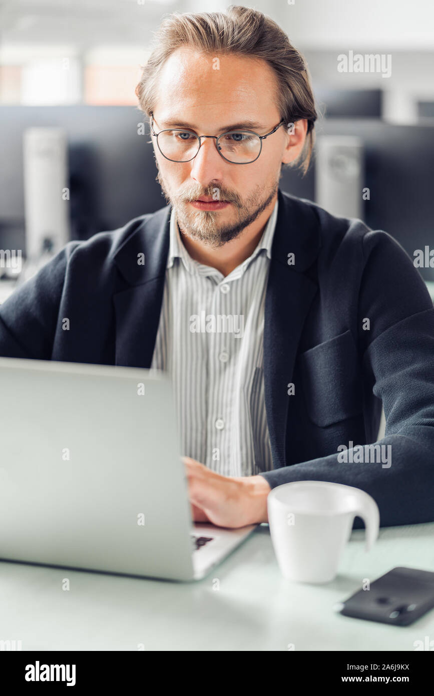 Young Man Sitting By The Desk Working On A Computer Blurred Computer Work Stations In The