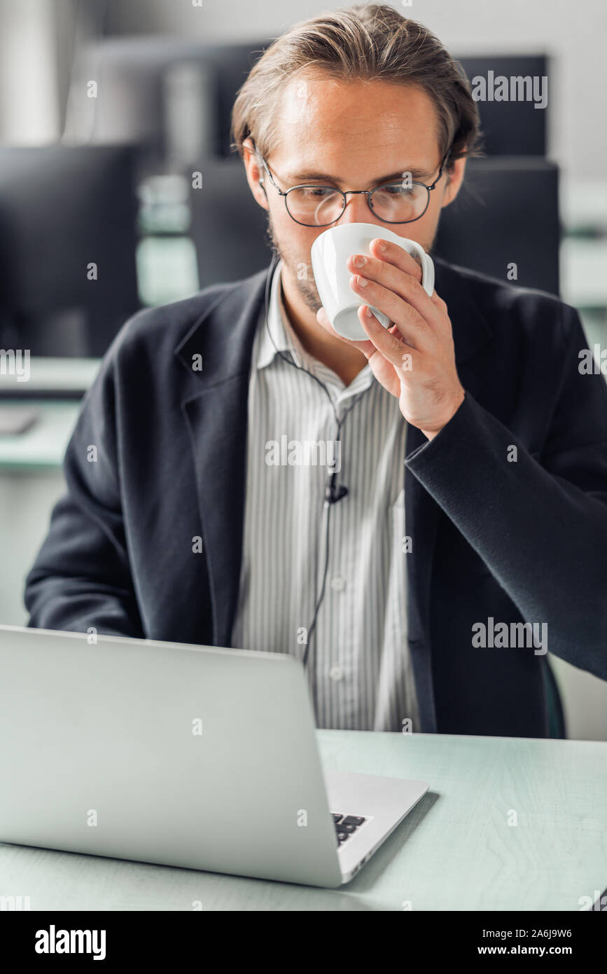 Young handsome man drinking coffee while working by the computer ...