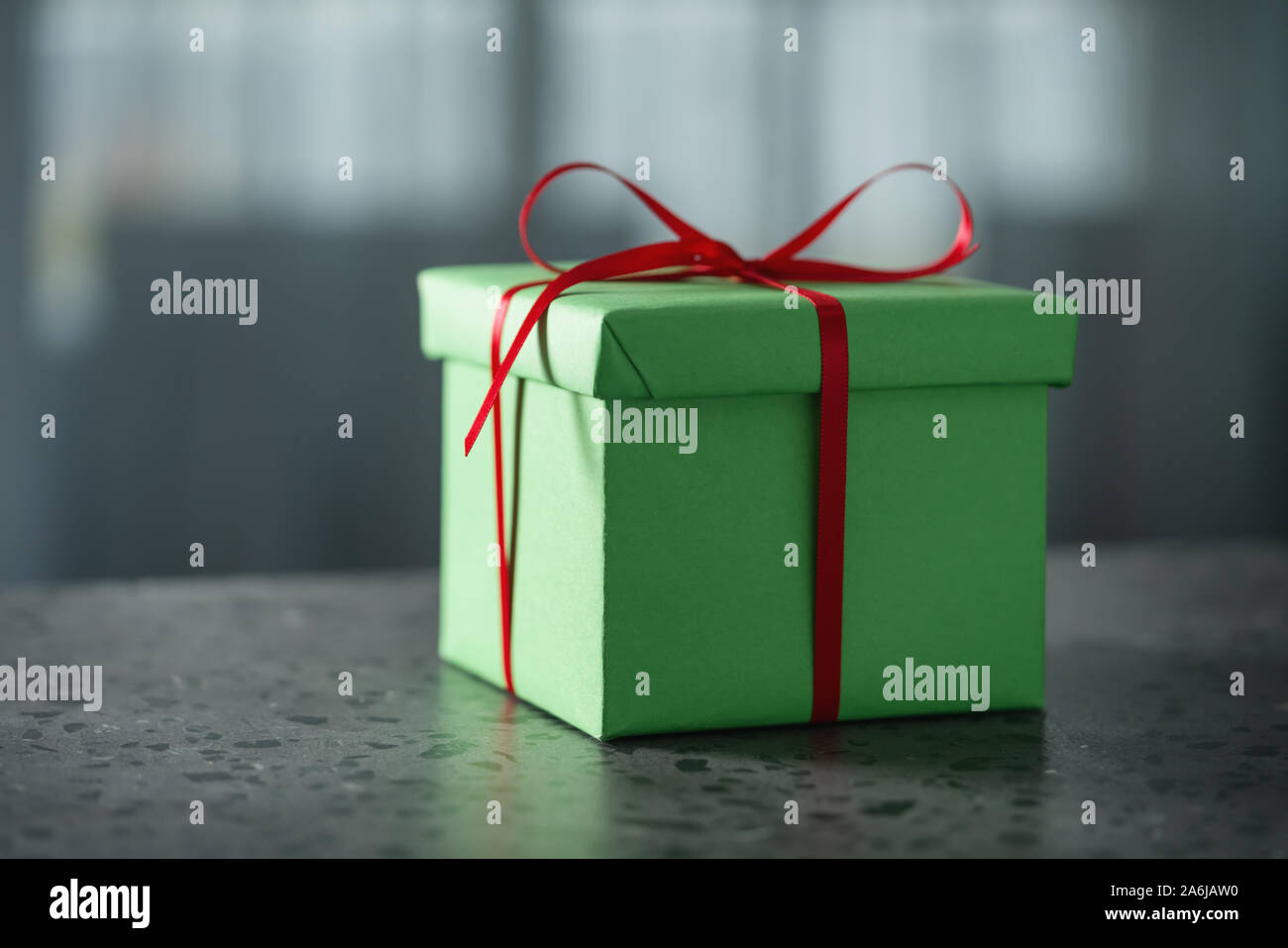 Green gift box with red ribbon against window on terrazo countertop ...