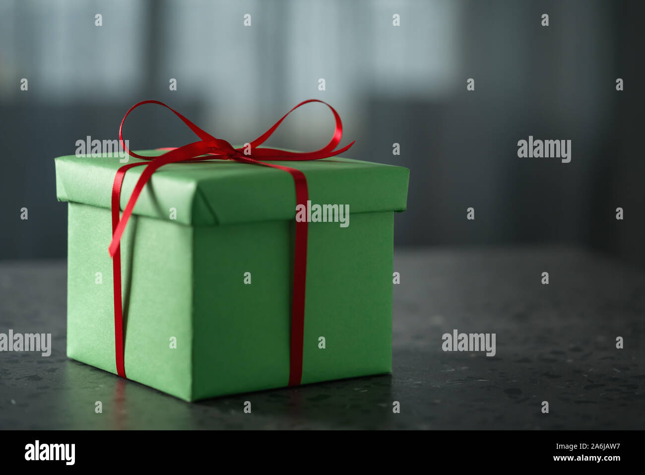 Green gift box with red ribbon against window on terrazo countertop ...