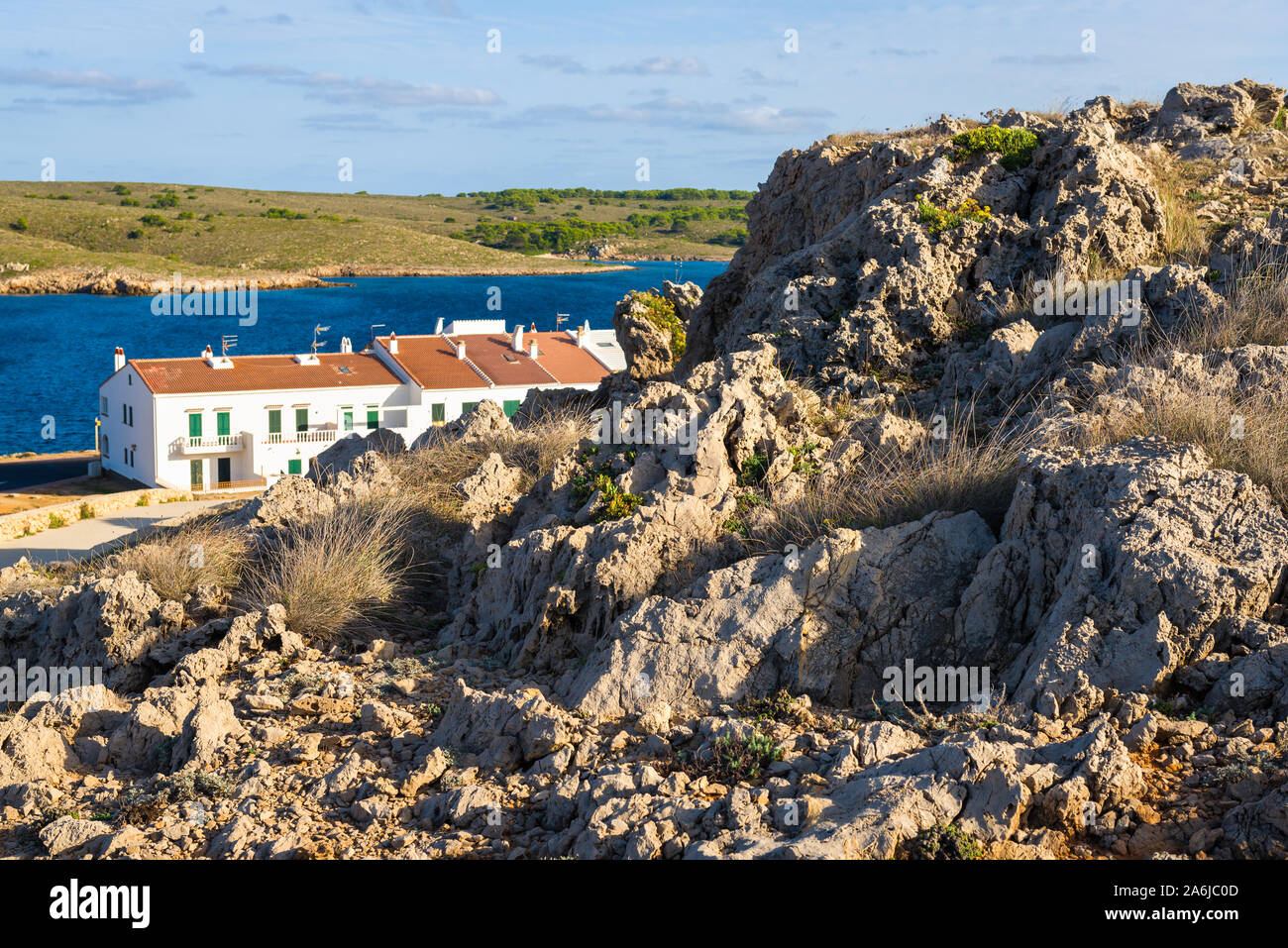 Rocks with a view of bay and buildings of Fornells village in Menorca ...