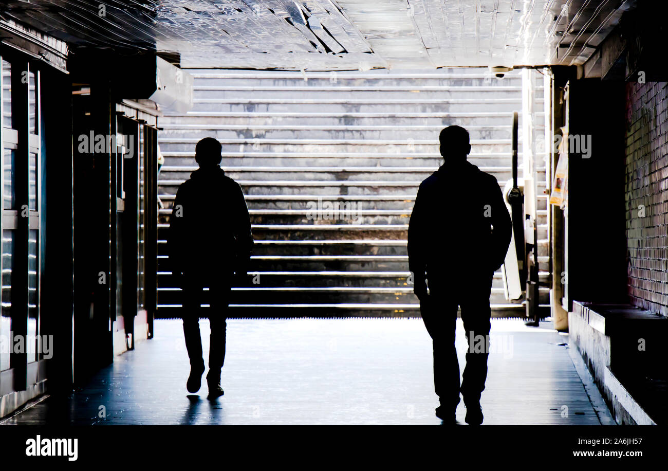 Two men walking in subway walkway passage in high contrast black and ...