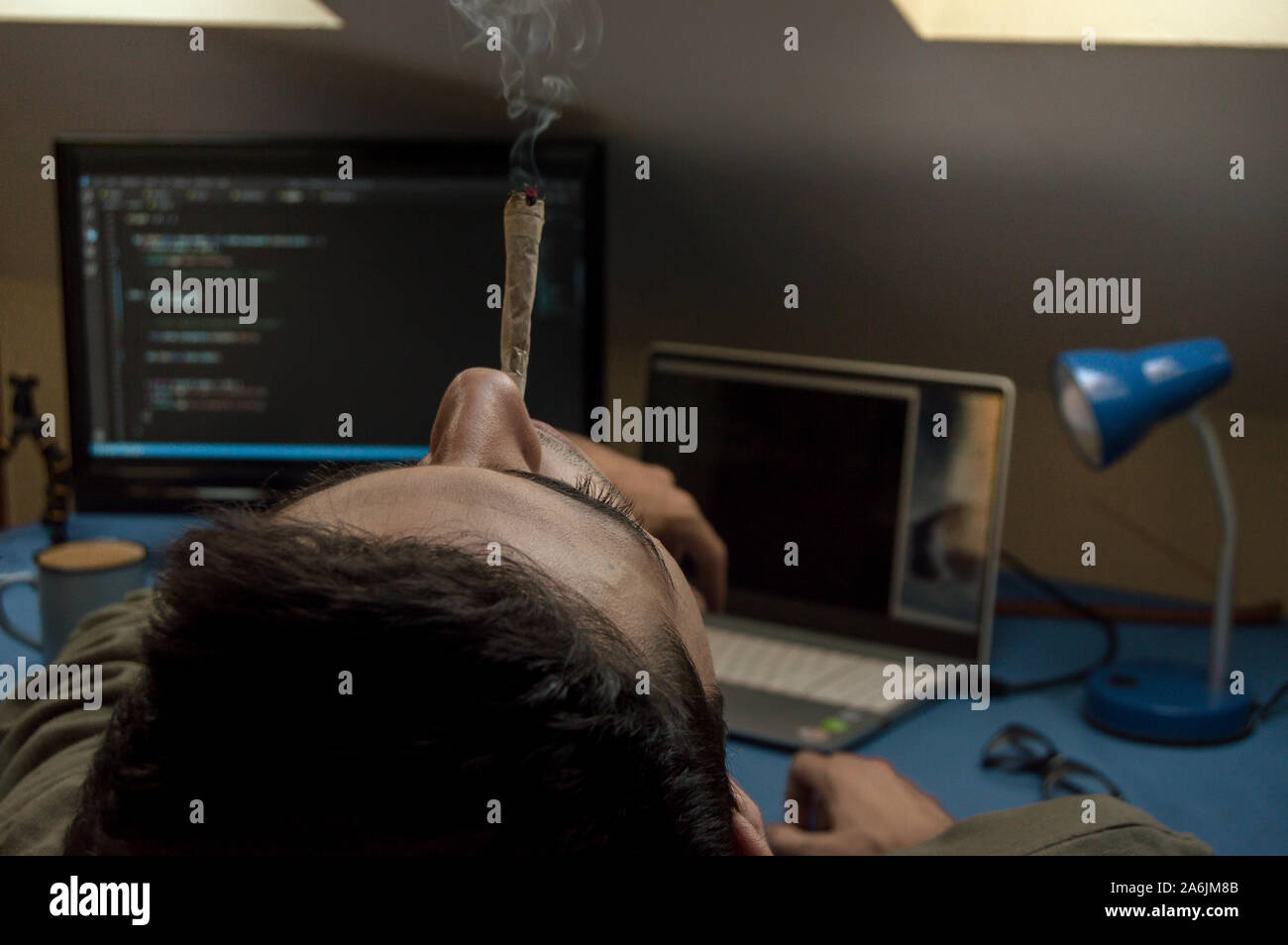 Young man smoking a marijuana joint at home while working with ...